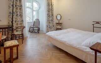 Quarto com cama, uma cadeira, mesa pequena e espelho.