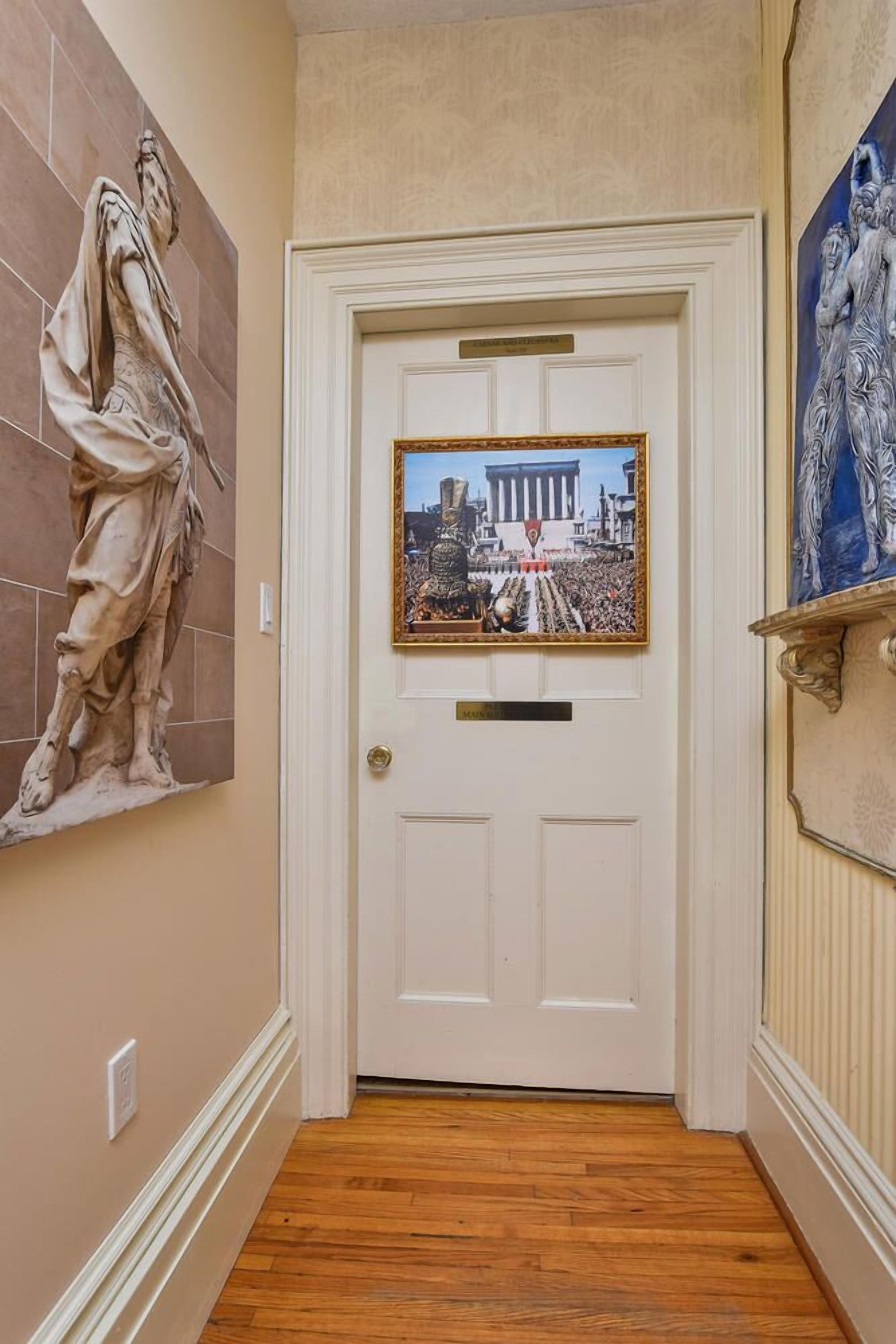 Um corredor com uma porta branca, um quadro de um edifício histórico e uma estátua na parede.