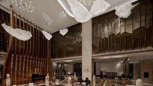 Um hall amplo com pé-direito alto, luminárias modernas e diversas opções de assentos, incluindo sofás e mesas.