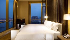 Quarto de hotel com uma cama grande, televisão, telefone e vista da cidade à noite.