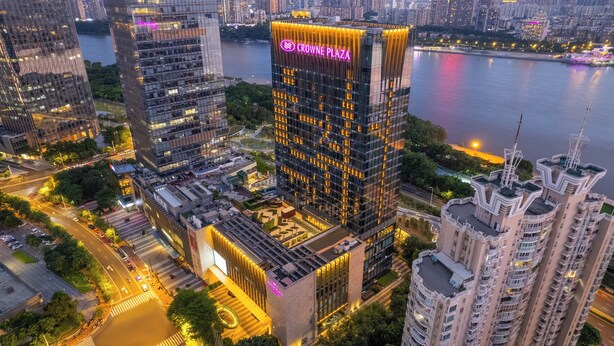 Um edifício alto com um letreiro chamativo 'Crowne Plaza', cercado por outros edifícios e um corpo d'água.