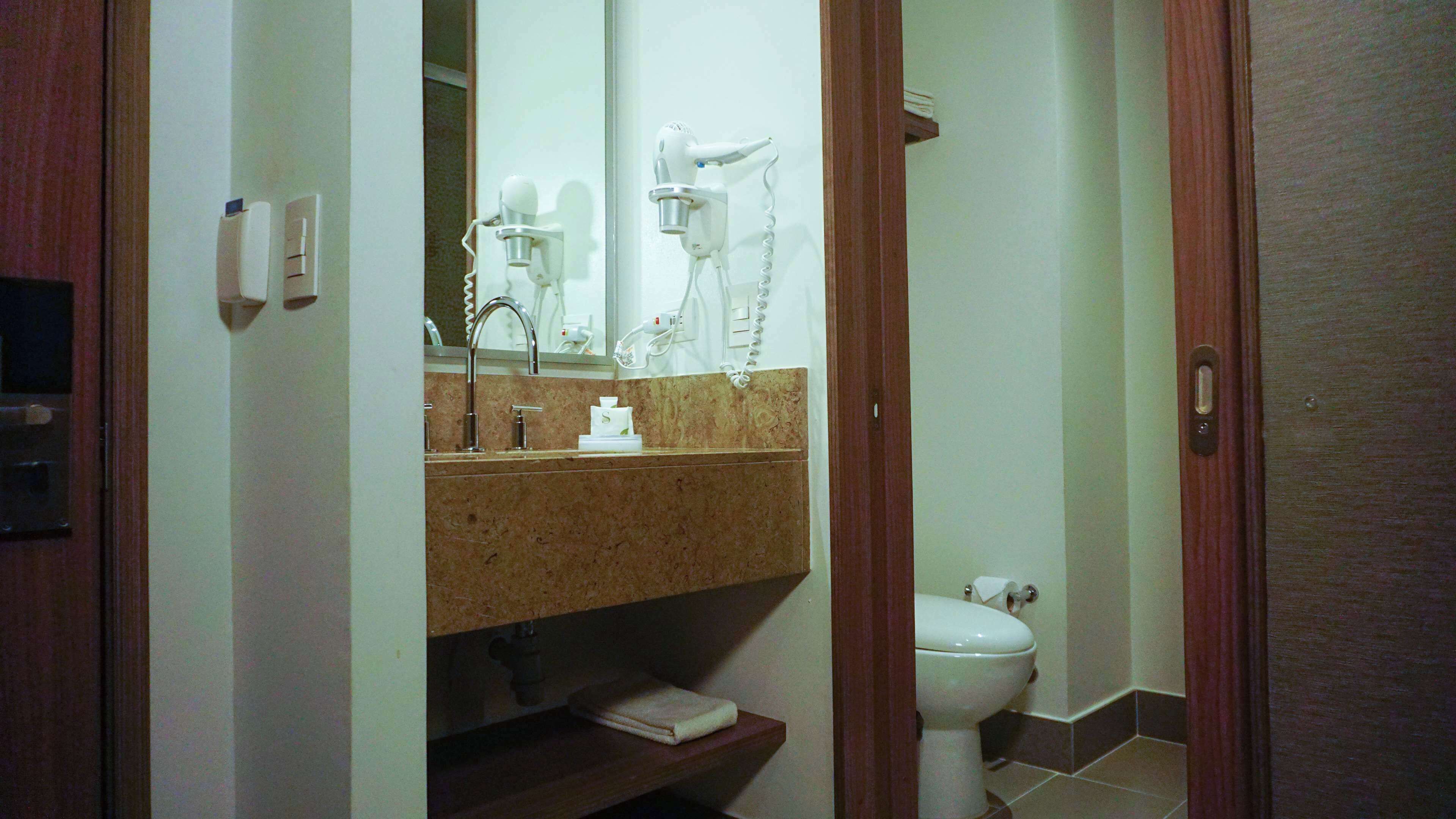 Casa de banho com lavatório, espelho, porta-toalhas e secador de cabelo.