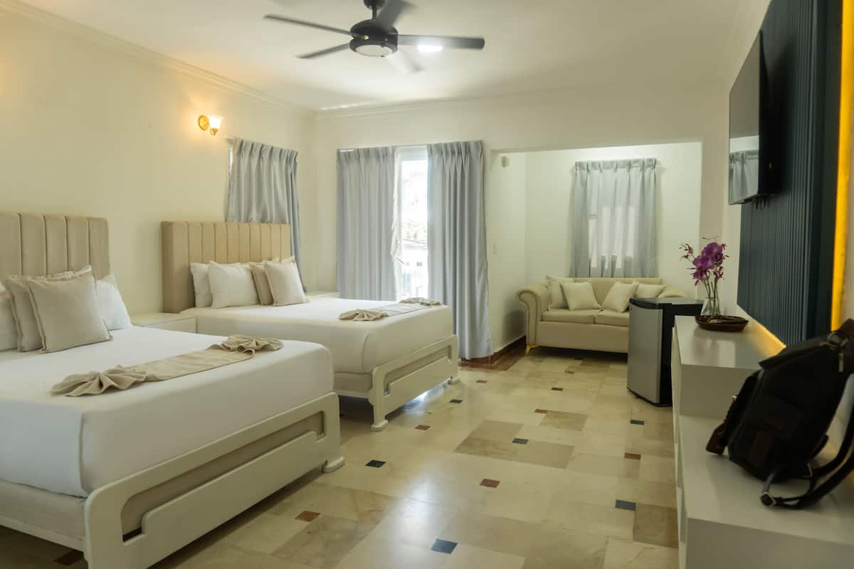 Quarto de hotel com duas camas, uma escrivaninha, uma cadeira, uma televisão e um ventilador de teto.