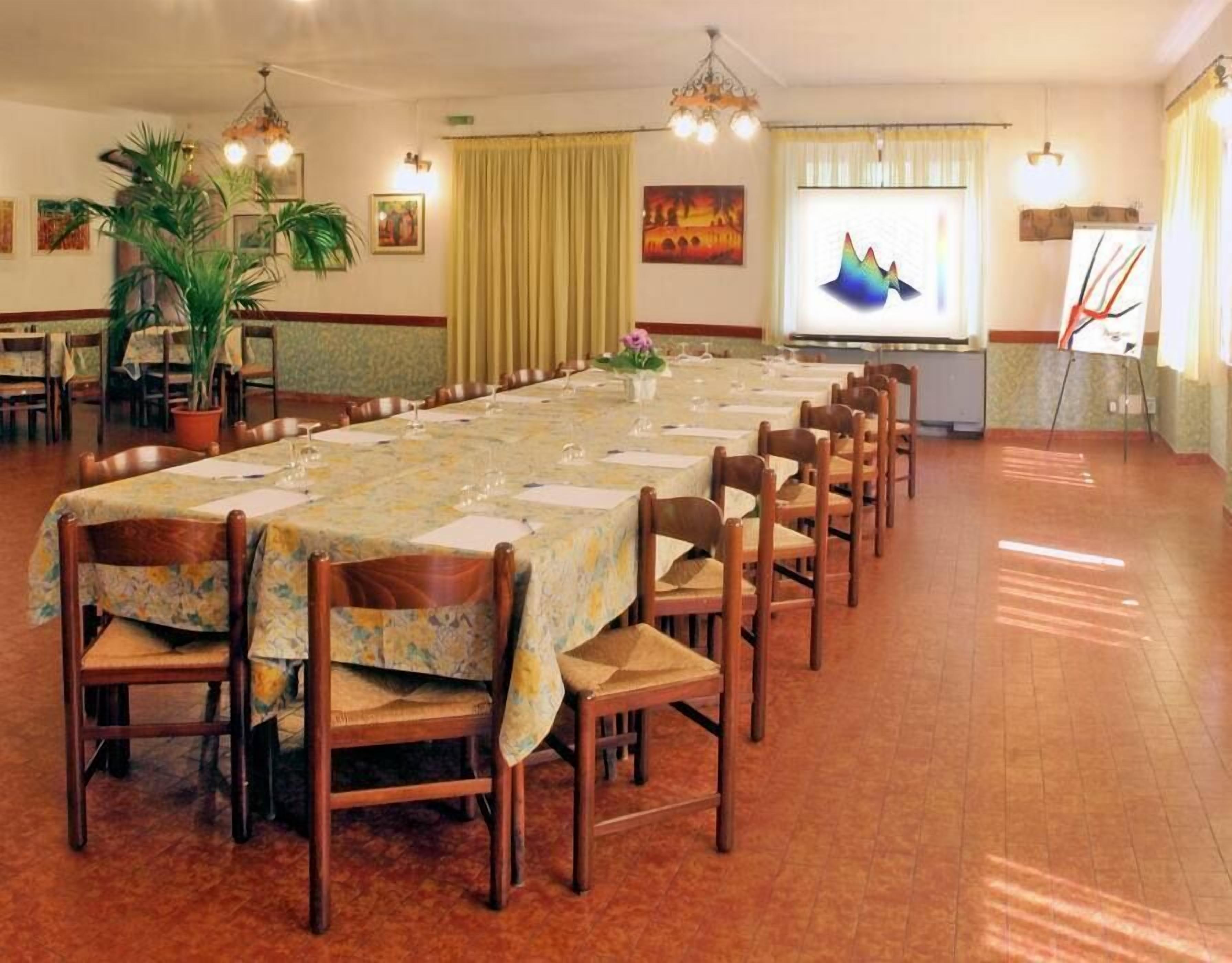 Uma longa mesa de jantar com cadeiras, uma planta em vaso e obras de arte nas paredes.