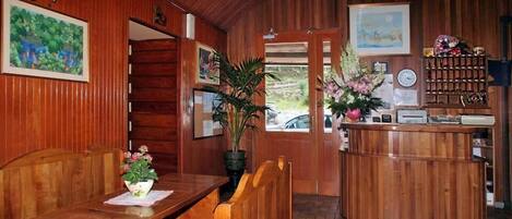 Um interior em madeira com um balcão de recepção, bancos de madeira e uma planta em vaso.