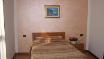 Quarto com cama de madeira, quadro pendurado na parede e mesa de cabeceira com um cesto de flores.