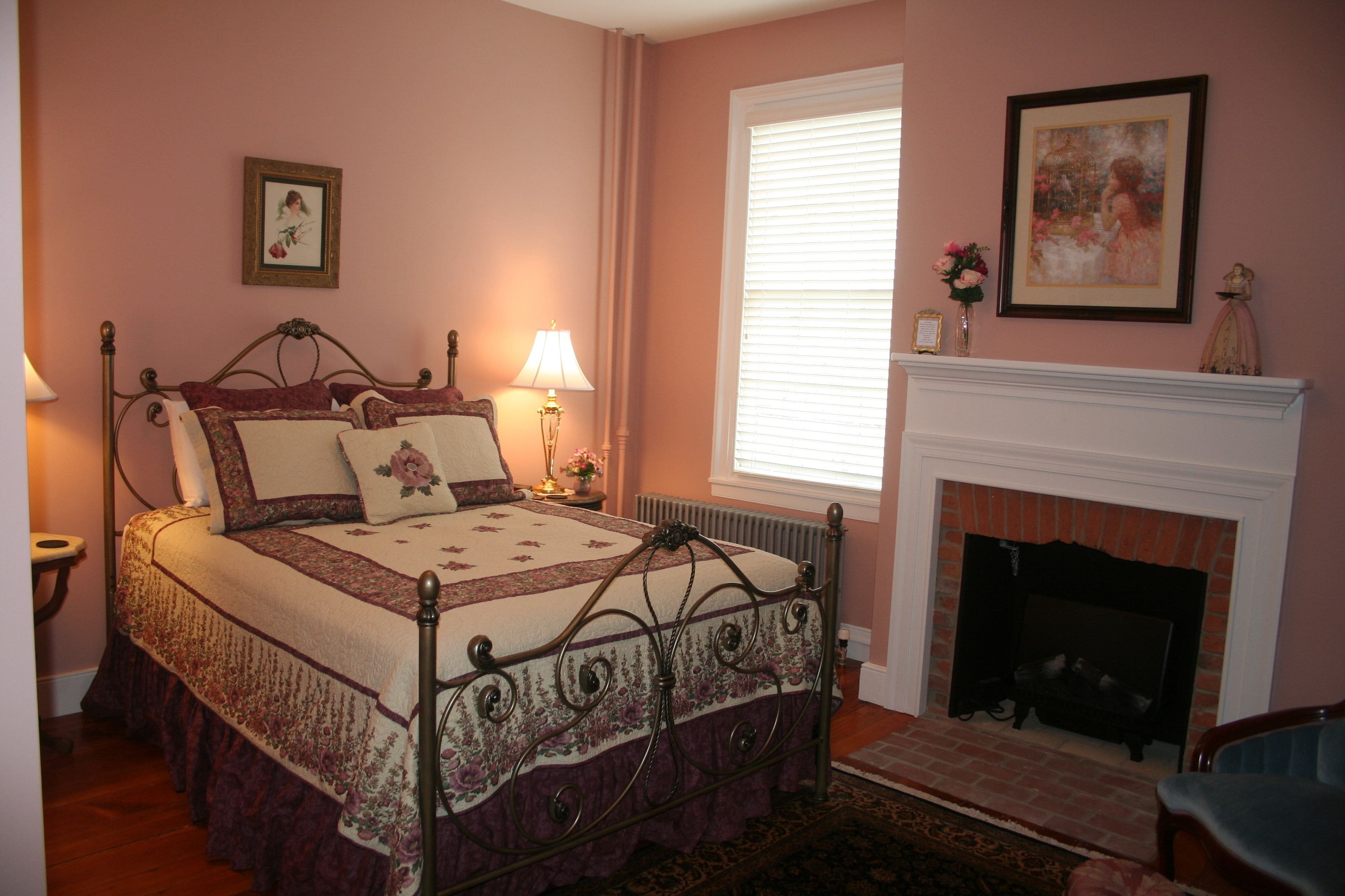 Um quarto com uma cama de dossel, lareira, janela com persianas e um quadro na parede.