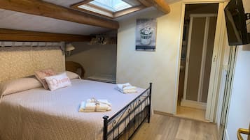 Quarto com cama, claraboia, televisão fixada na parede e porta para outro cômodo.