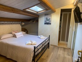Quarto com cama, claraboia, televisão fixada na parede e porta para outro cômodo.