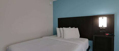 Quarto de hotel com uma cama de solteiro, mesa de cabeceira com abajur e parede azul decorativa.