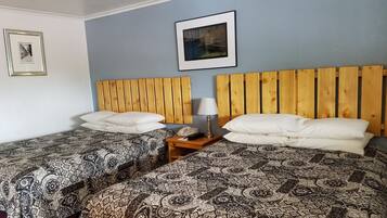 Quarto com duas camas, cada uma com roupa de cama estampada e cabeceira de madeira. Há um quadro na parede e uma mesa de cabeceira com uma luminária.