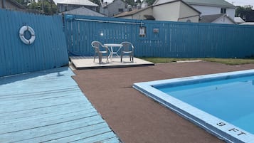 Um quintal com piscina, cerca azul e área de varanda com cadeiras e mesa.