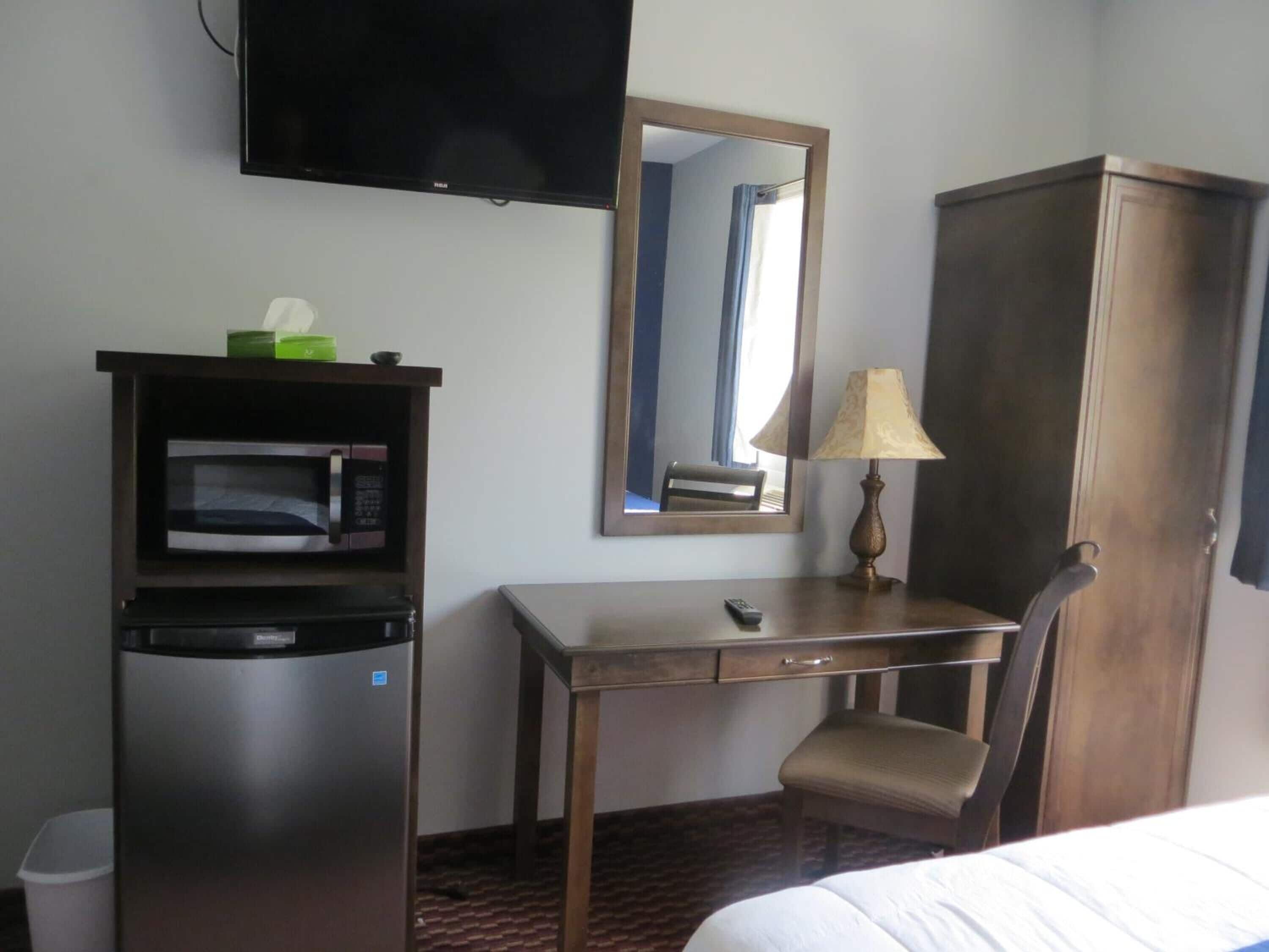 Quarto de hotel com cama, escrivaninha e cadeira, micro-ondas, televisão, espelho e guarda-roupa.