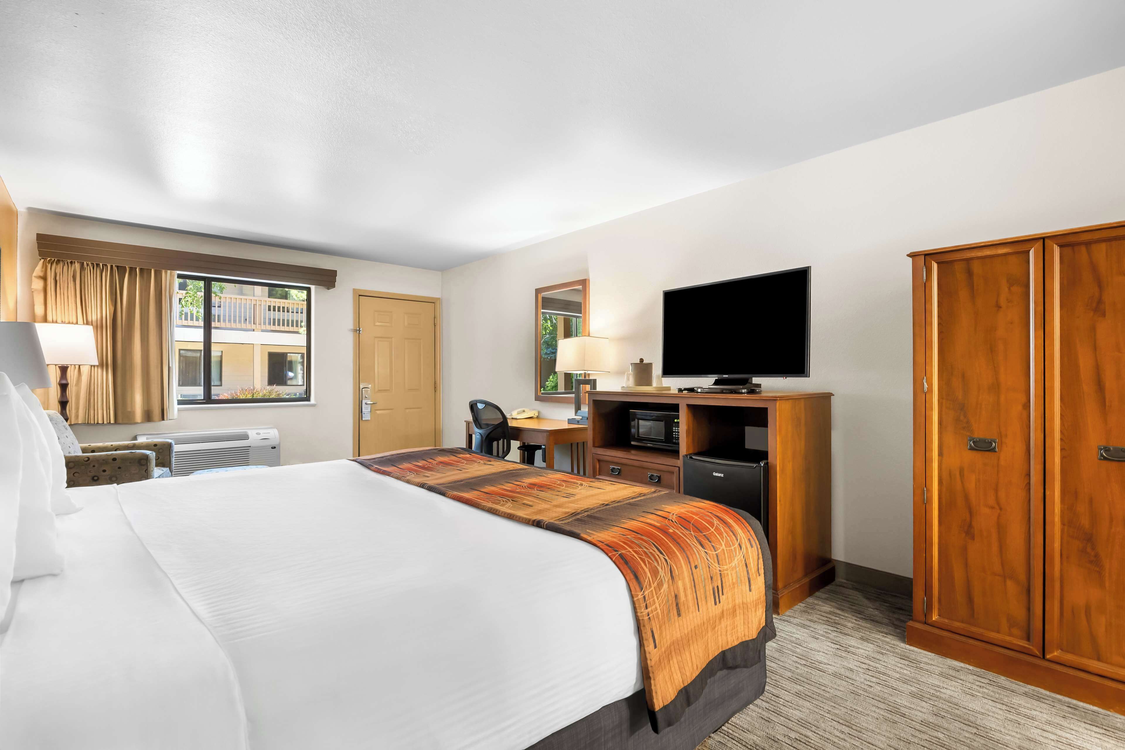 Quarto de hotel com uma cama grande, uma escrivaninha com computador, uma televisão e um guarda-roupa.