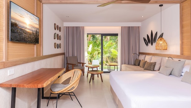 Quarto de hotel com uma cama, uma escrivaninha, uma cadeira, uma mesinha e vista para o verde pela janela.