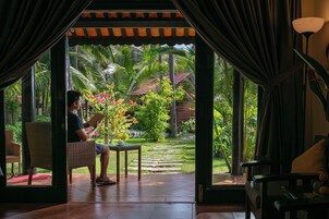 Quarto com vista para um jardim, uma pessoa lendo e uma mesa com uma cadeira.