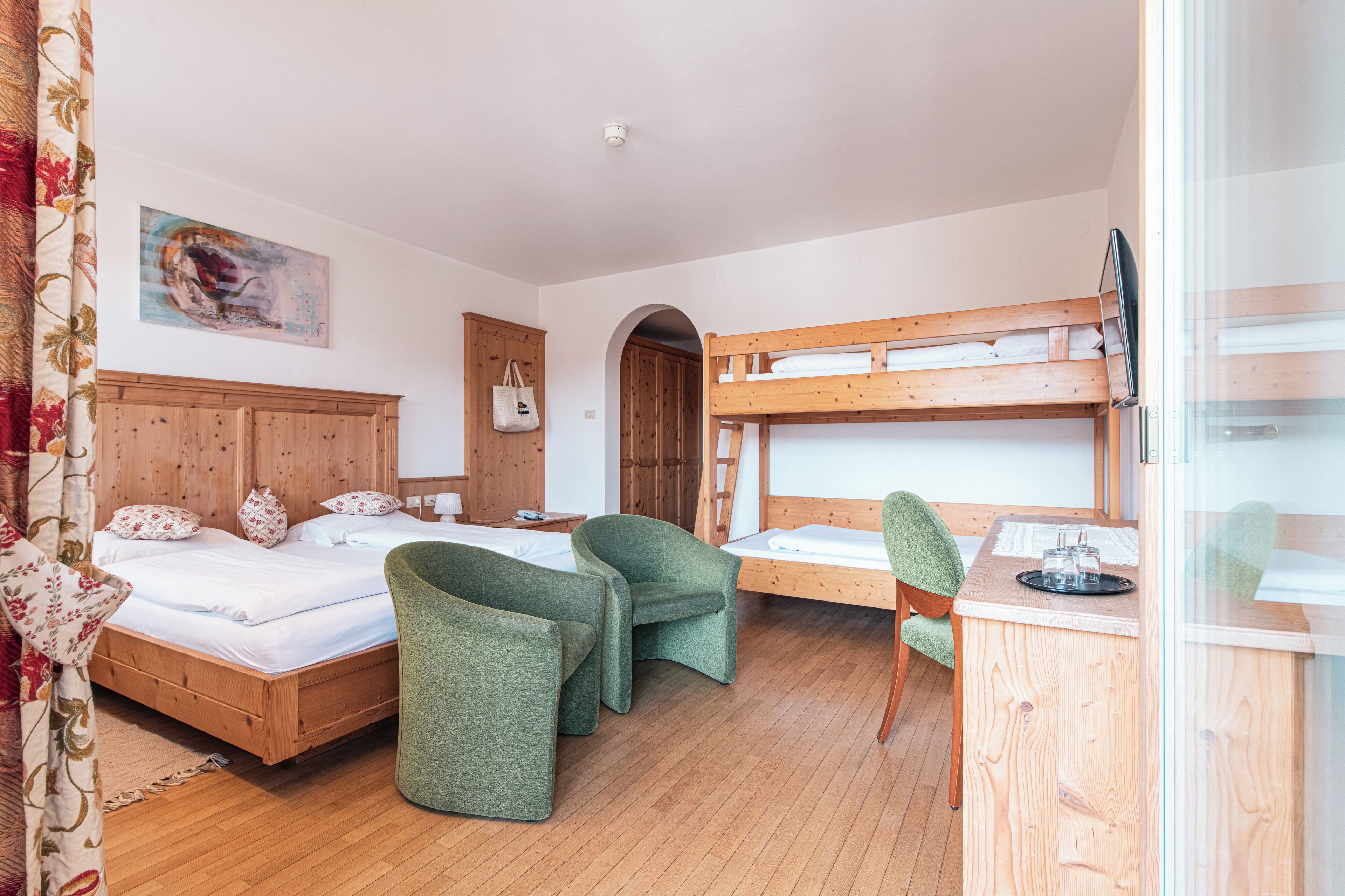 Um quarto com uma cama de beliche, duas cadeiras verdes, uma escrivaninha de madeira e um guarda-roupa de madeira.