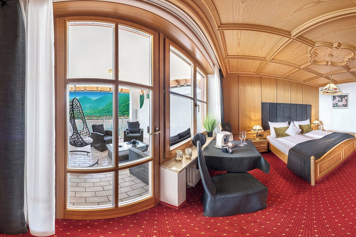 Quarto de hotel com uma janela grande, cama, escrivaninha e televisão.