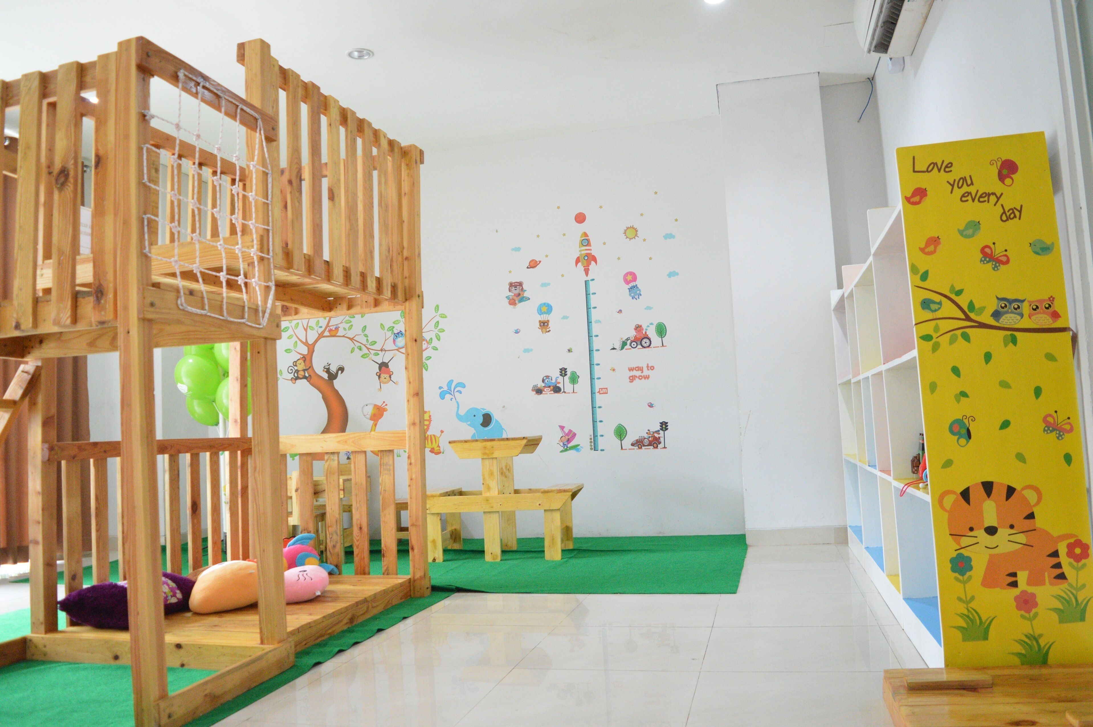 Espaço infantil com estrutura de escalada de madeira, tapete verde e parede decorada com adesivos educativos.