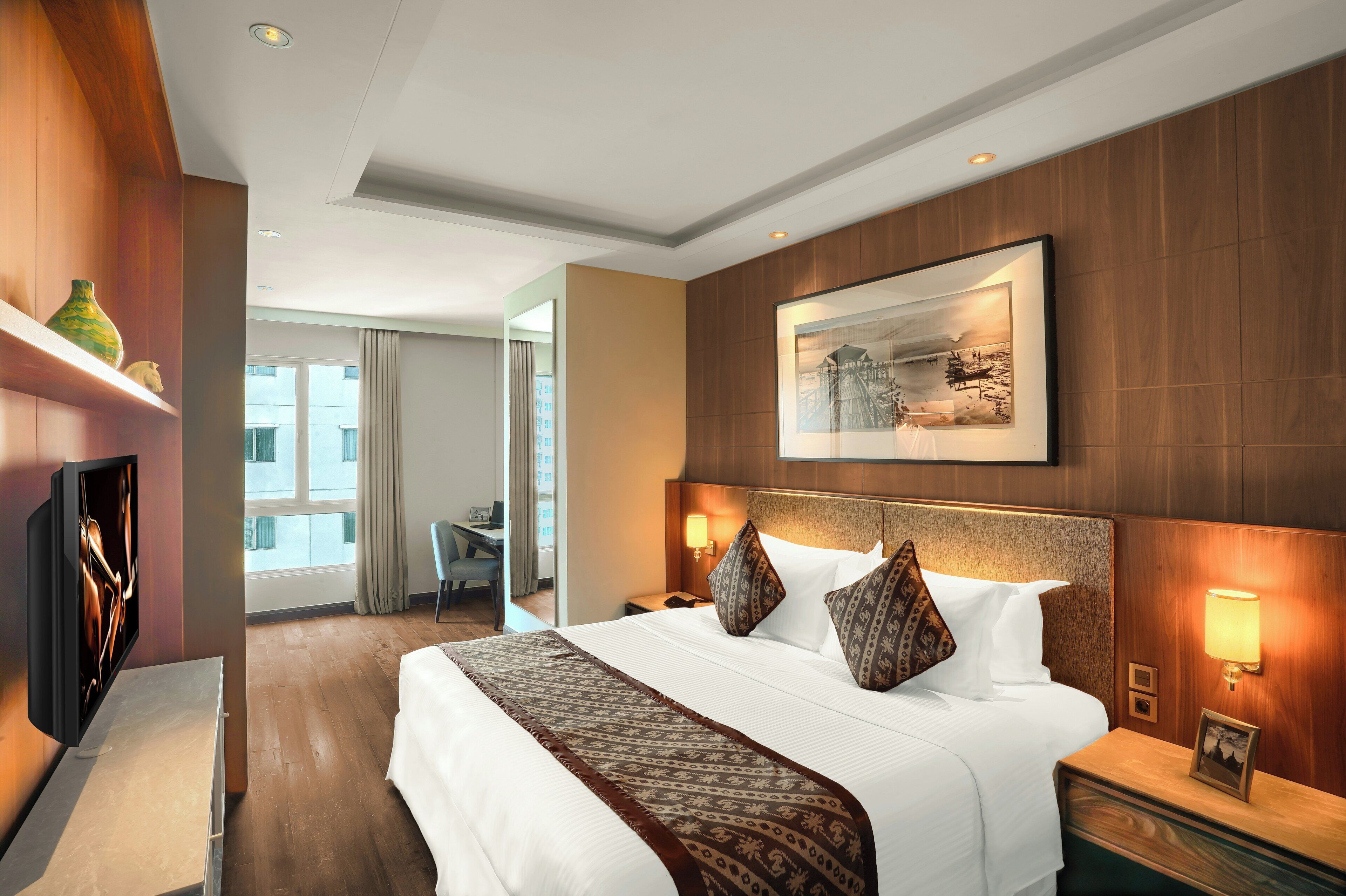 Quarto de hotel com uma cama grande, televisão de tela plana, escrivaninha e janela com cortinas.