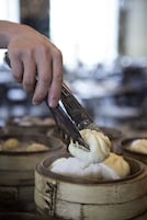 Uma mão usando pinças para manusear um alimento em um cozedor de bambu.