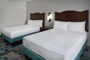 Quarto de hotel com duas camas, uma mesinha de cabeceira e um aplique na parede.