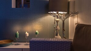 Um quarto com parede texturizada, uma mesa com velas, um abajur e um vaso decorativo.