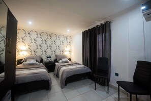 Quarto com duas camas, uma mesinha de cabeceira, uma cadeira e papel de parede estampado.