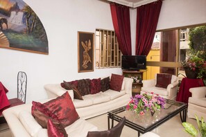 Uma sala de estar com sofá, poltronas, mesa de centro com flores, televisão e um quadro na parede.