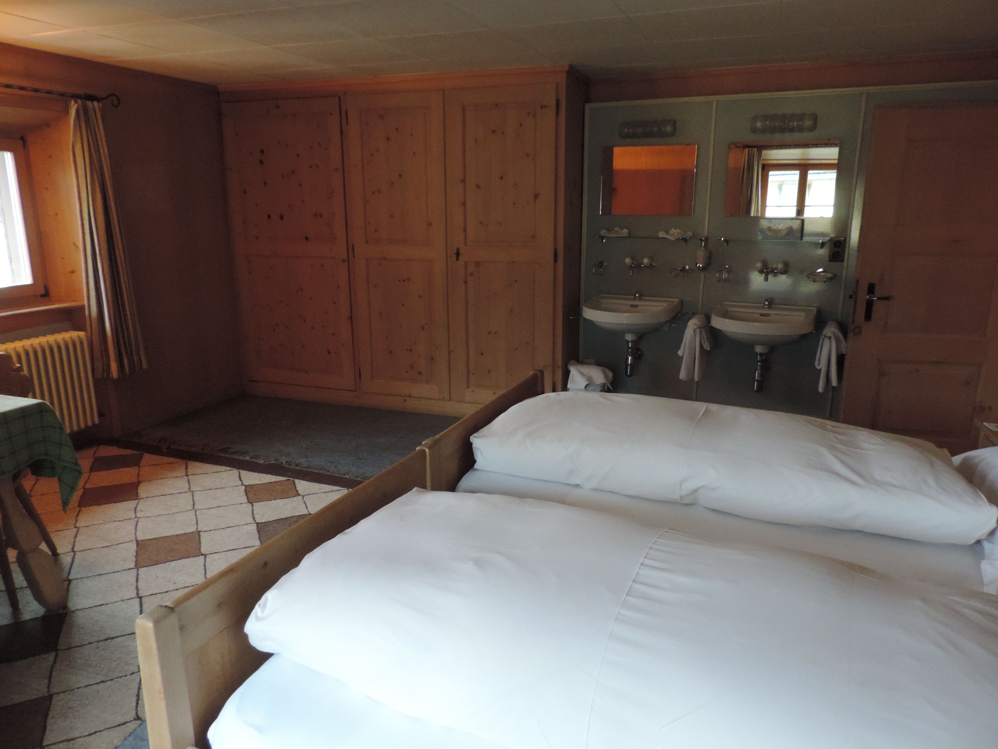 Quarto com cama, guarda-roupa de madeira, duas pias e janela com cortinas.