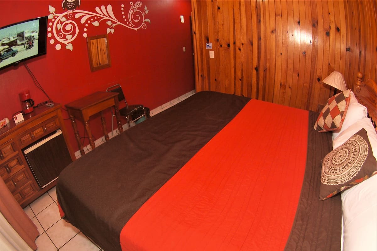 Quarto com uma cama, painéis de madeira, televisão, escrivaninha e uma cadeira.