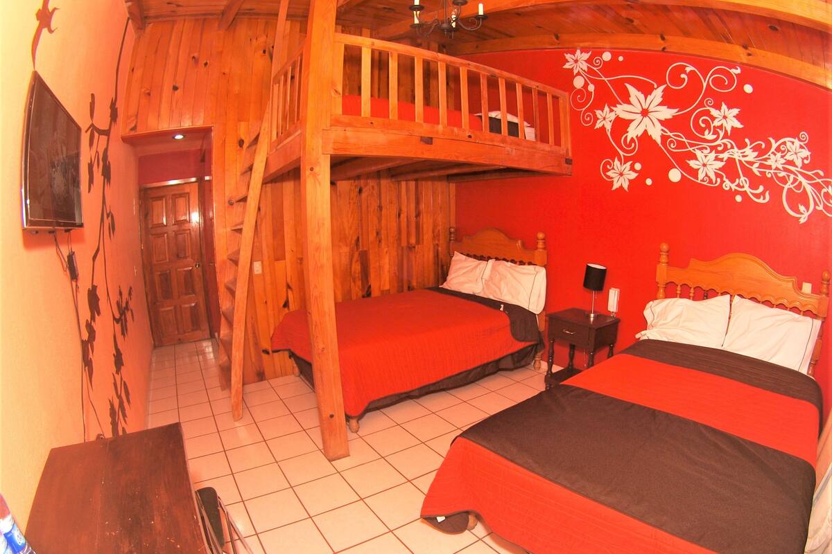 Uma cabana de madeira com duas camas, um lance de escadas e uma parede vermelha decorada com motivos florais.