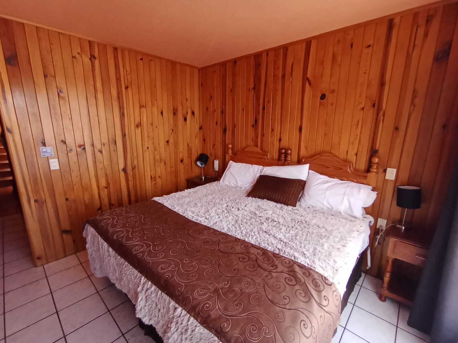 Quarto com painéis de madeira, uma cama grande, uma mesa de cabeceira e um abajur.