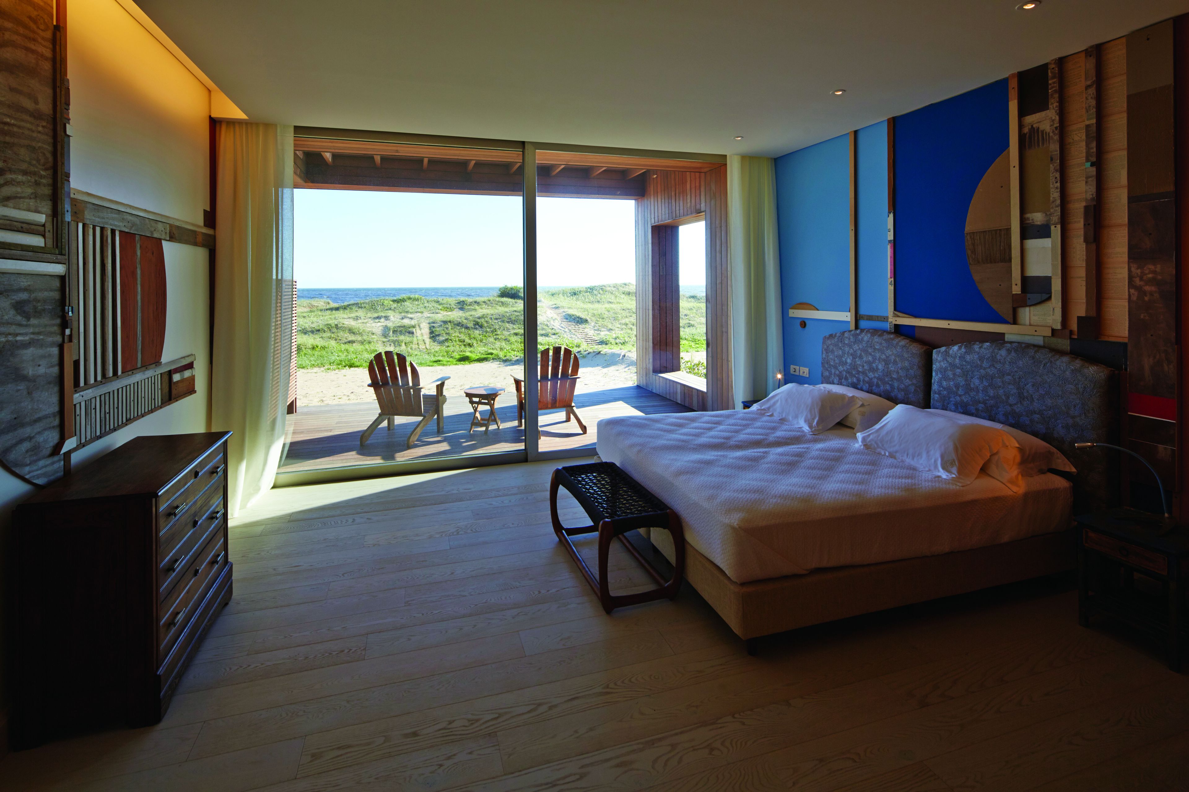 Quarto com cama grande, escrivaninha e cadeira. Vista para a praia pela janela.