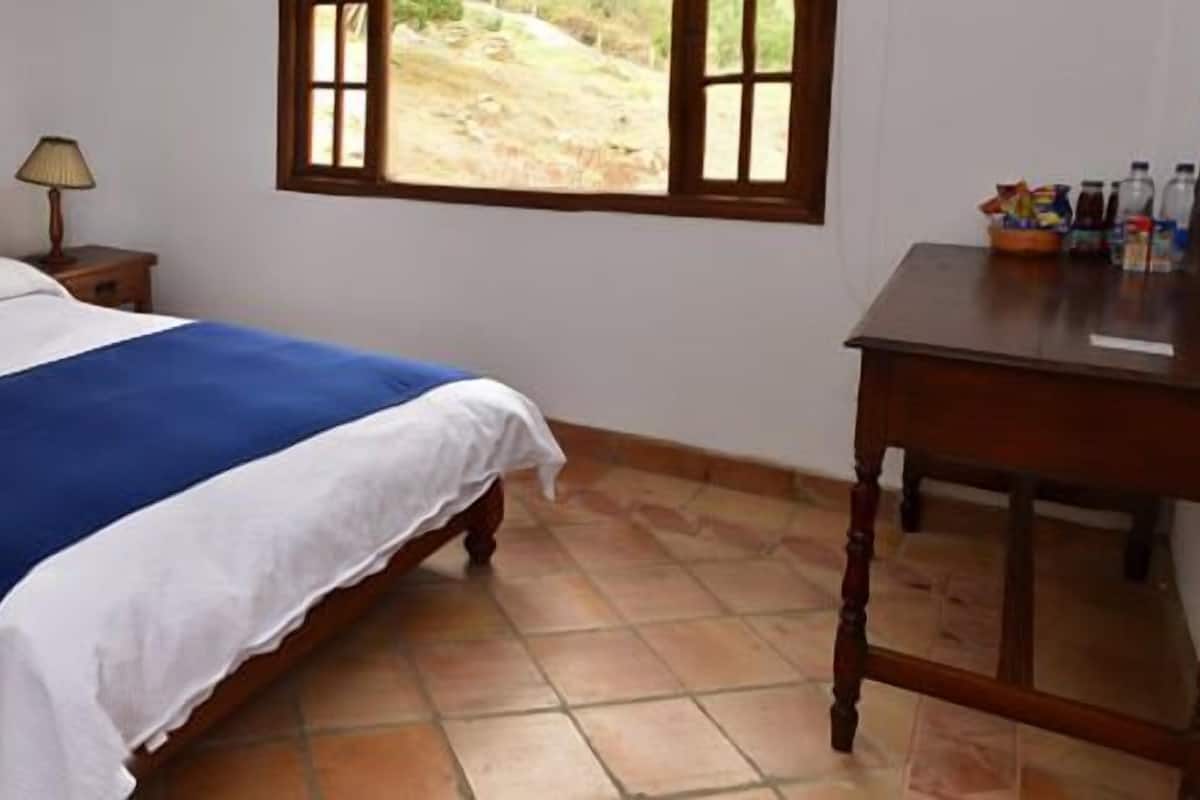 Quarto com cama de madeira, mesa de cabeceira, luminária, janela com vista e cômoda de madeira.