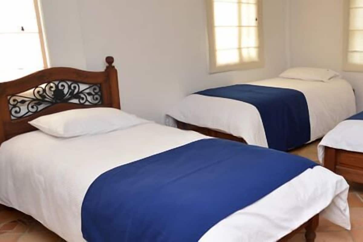 Quarto com três camas de solteiro, cada uma com cabeceira de madeira e roupa de cama branca.