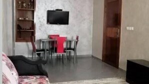 Uma sala de estar com sofá, televisão na parede, mesa de jantar com cadeiras e um armário de madeira.
