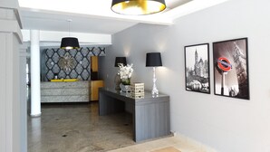 Um interior moderno com um balcão de recepção, uma parede decorativa com papel de parede estampado e duas imagens emolduradas de pontos turísticos de Londres.