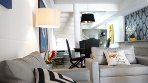 Uma sala de estar moderna com um sofá cinzento, uma cadeira preta e um espaço de jantar com mesa e cadeiras.