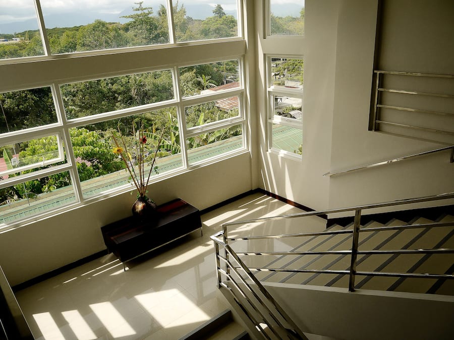 Escada com guarda-corpo de metal e vista para o verde através de grandes janelas.