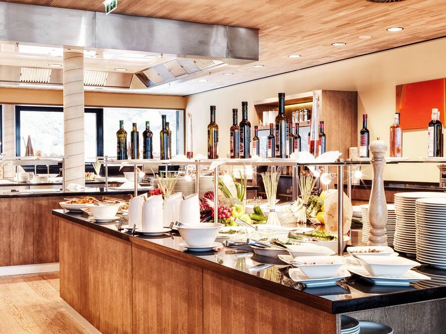 Uma área de buffet com diversas opções de comida, incluindo saladas, frutas e bebidas, dispostas sobre um balcão de madeira.