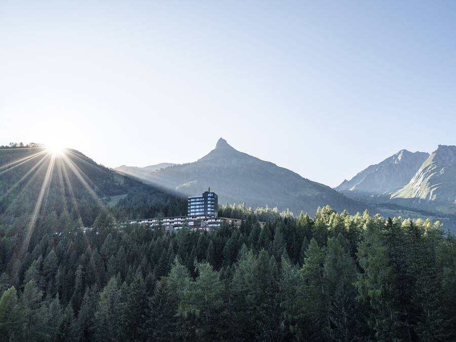 Uma pousada de montanha com design moderno, rodeada por uma floresta densa e montanhas.