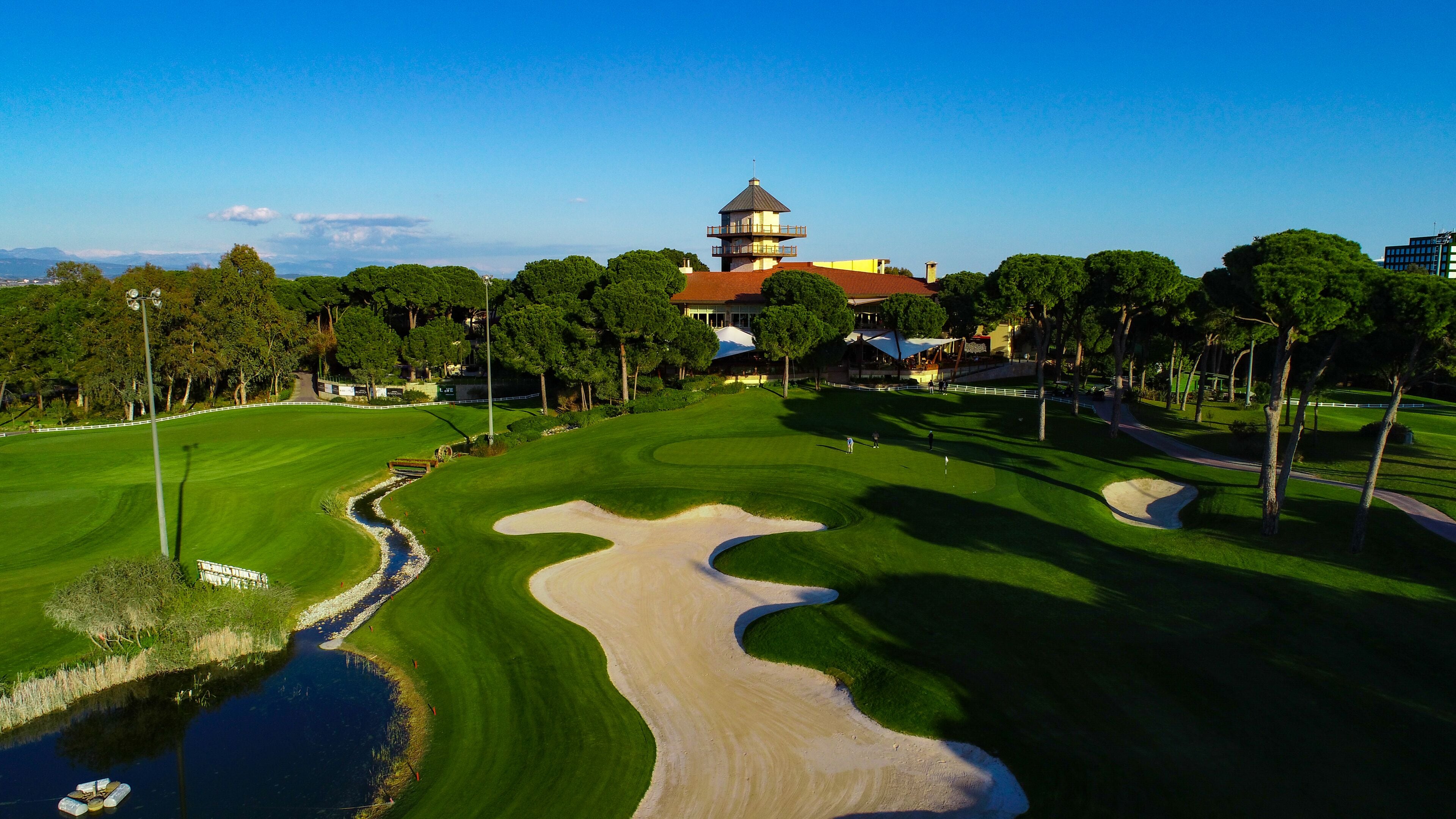 Um campo de golfe com bunkers de areia, um obstáculo aquático e um edifício em estilo pagode ao fundo.