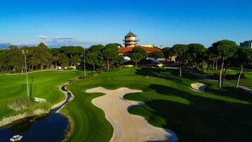 Um campo de golfe com bunkers de areia, um obstáculo aquático e um edifício em estilo pagode ao fundo.