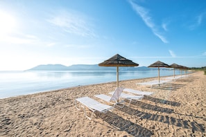 Uma praia com cadeiras de praia brancas e toldos de palha.
