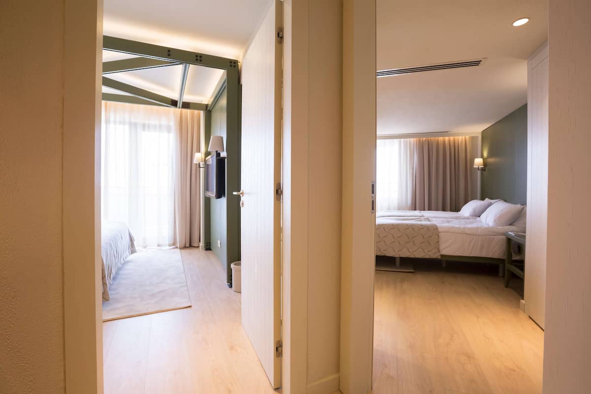 Quarto de hotel com cama, mesa de cabeceira, luminária e janela com cortinas.