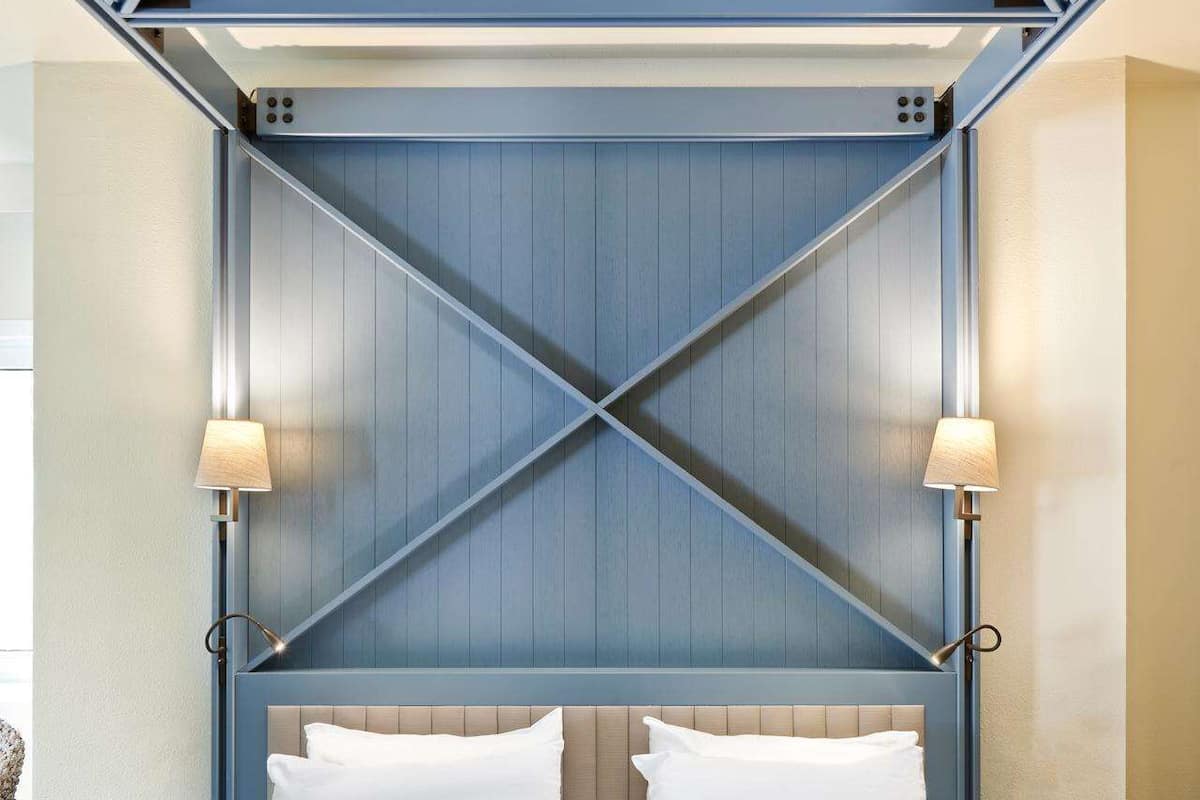 Uma cama com cabeceira de design cruzado, duas luminárias laterais e um edredom estampado.