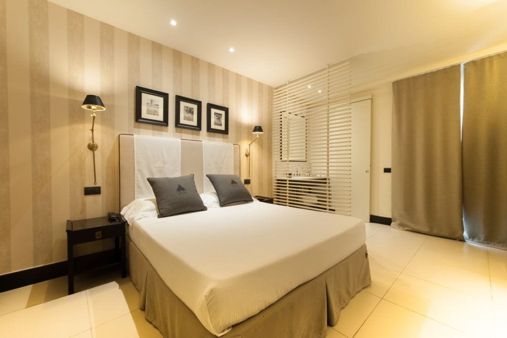 Quarto moderno com uma cama grande, duas luminárias de cabeceira, uma mesinha de cabeceira e um quadro na parede.