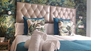 Quarto com cama grande, cabeceira estofada e papel de parede com padrão de folhagem tropical.
