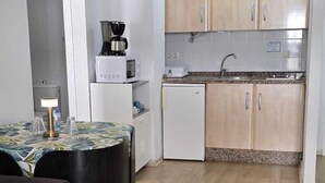 Um espaço compacto com cozinha americana, área de refeições com mesa e cadeiras, e área de estar com mesa de vidro e almofadas.